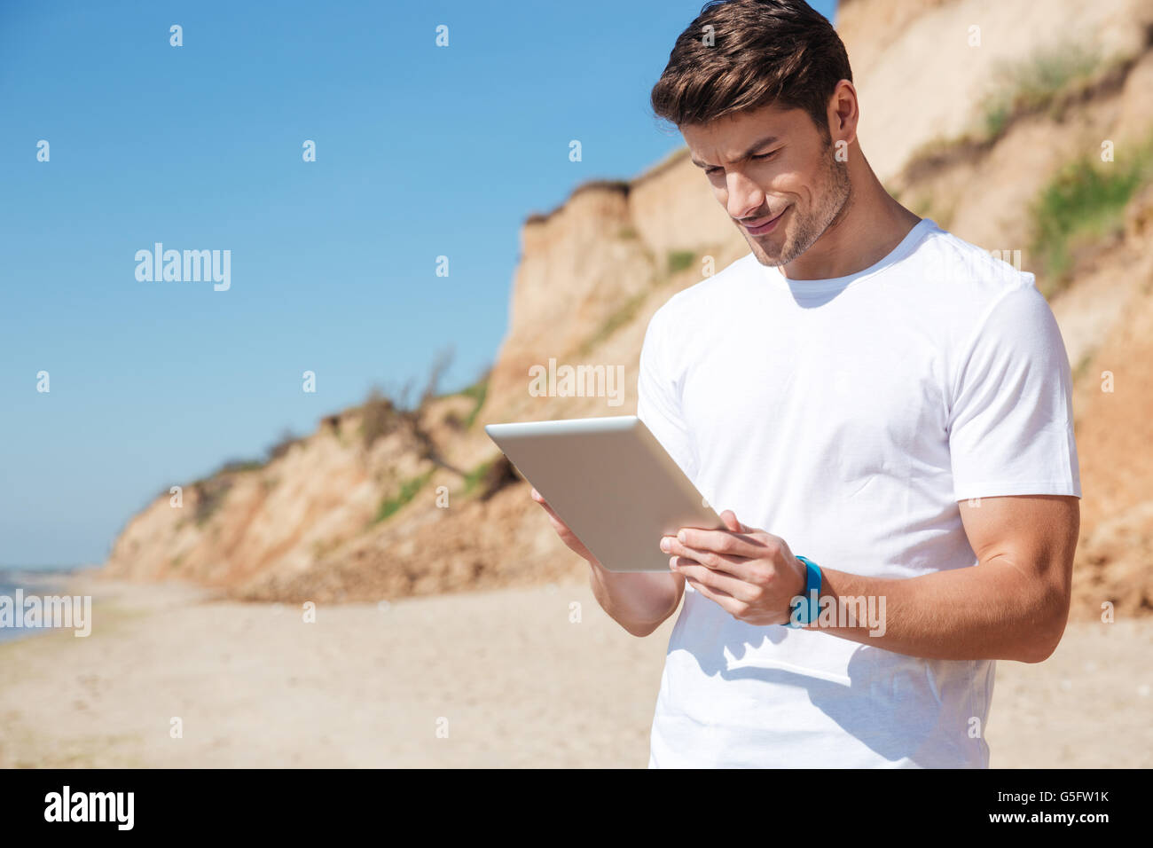 Happy young man holding and using tablet on the beach Stock Photo - Alamy