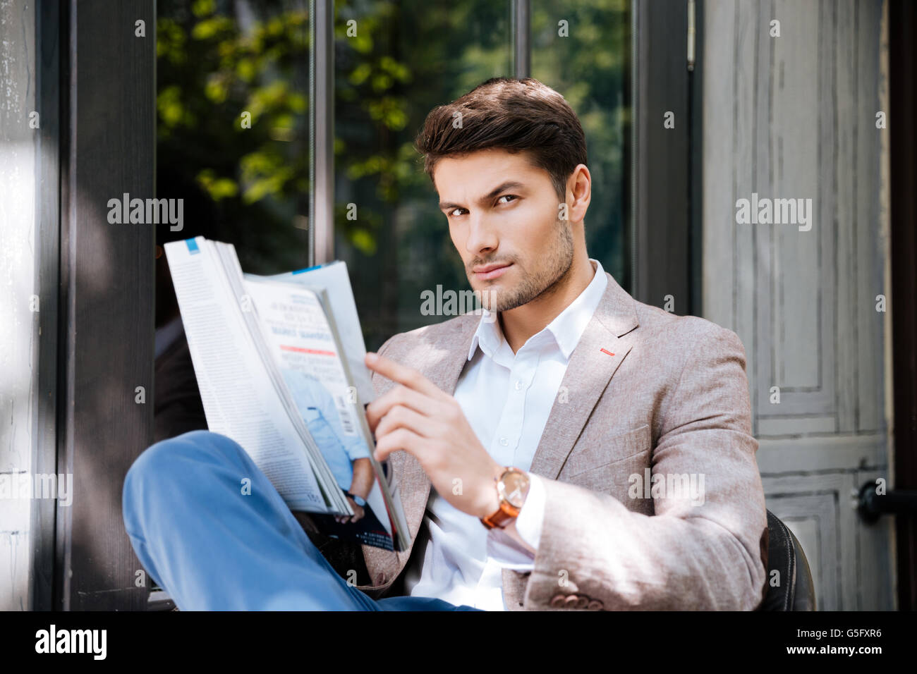 Attractive young man with magazine sitting in outdoor cafe Stock Photo ...