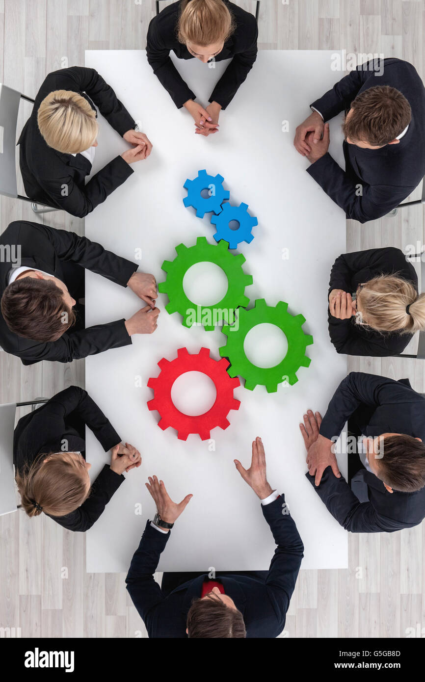 Business team sitting around the table with cogs, teamwork concept ...