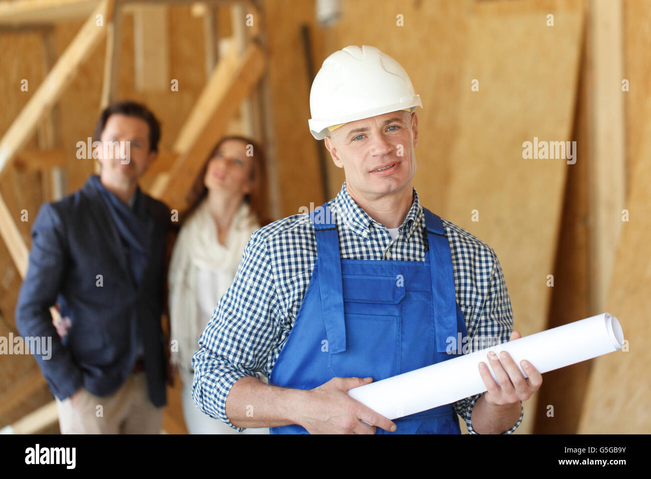 Worker holding house design plans and a young couple at construction ...