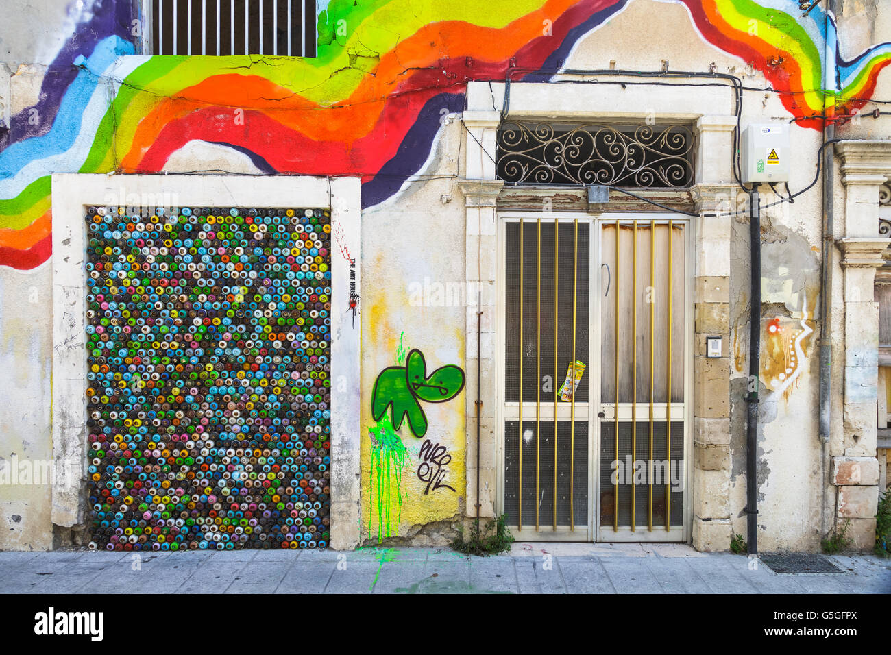 Rainbow graffiti on the old wall with gate full of aerosol cans ...