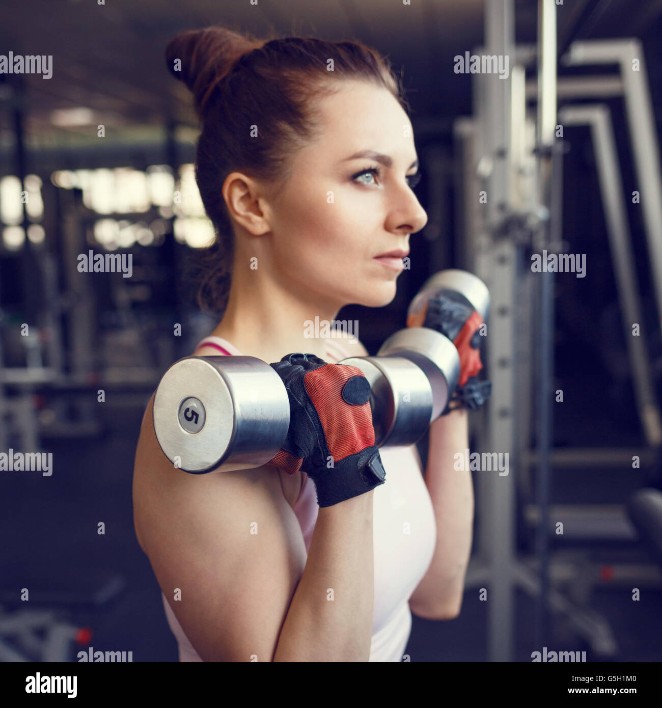 Young confident woman doing biceps curl exercise with dumbbells in ...