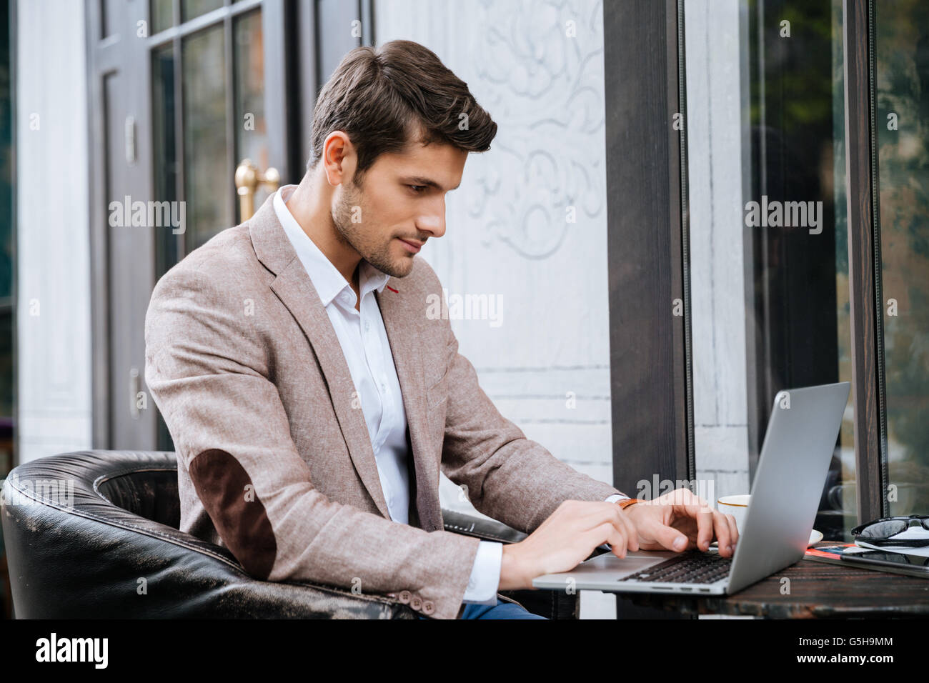 Concentrated young man sitting and using laptop in outdoor cafe Stock ...