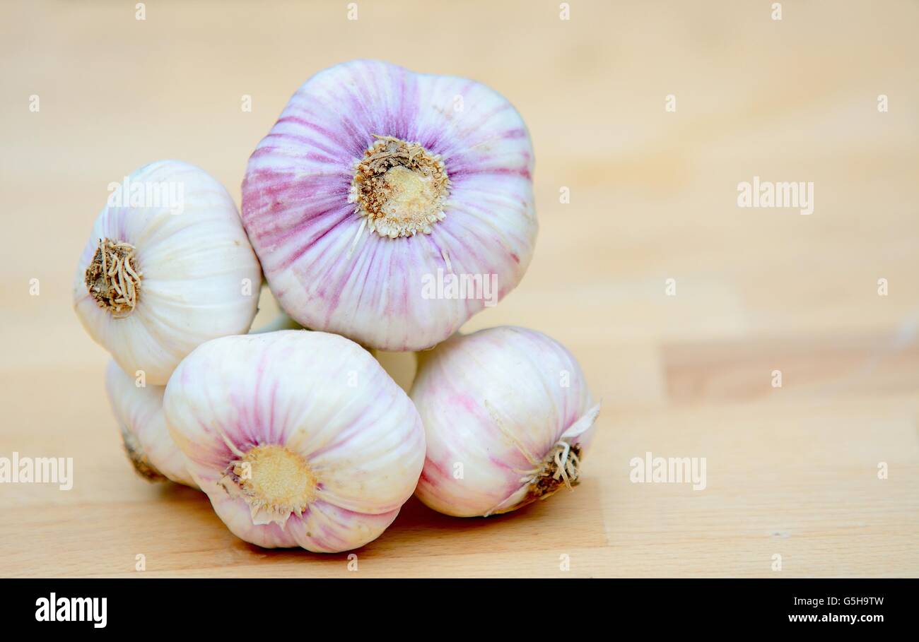 Bunch of fresh garlic with green scape on brown wood plate Stock Photo ...