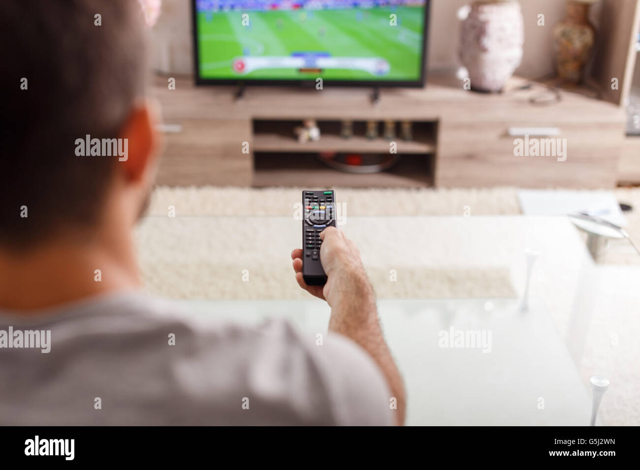 Man with remote control watching football match at home Stock Photo - Alamy