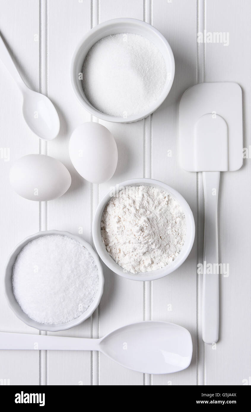 All white baking still life. Items include: spatula, whisk, eggs, flour ...