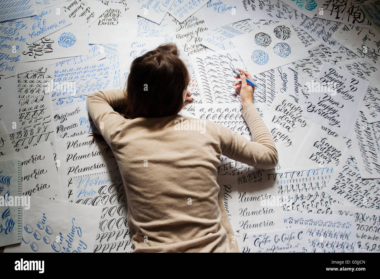 Beautiful young woman calligrapher writing something lying on the floor ...