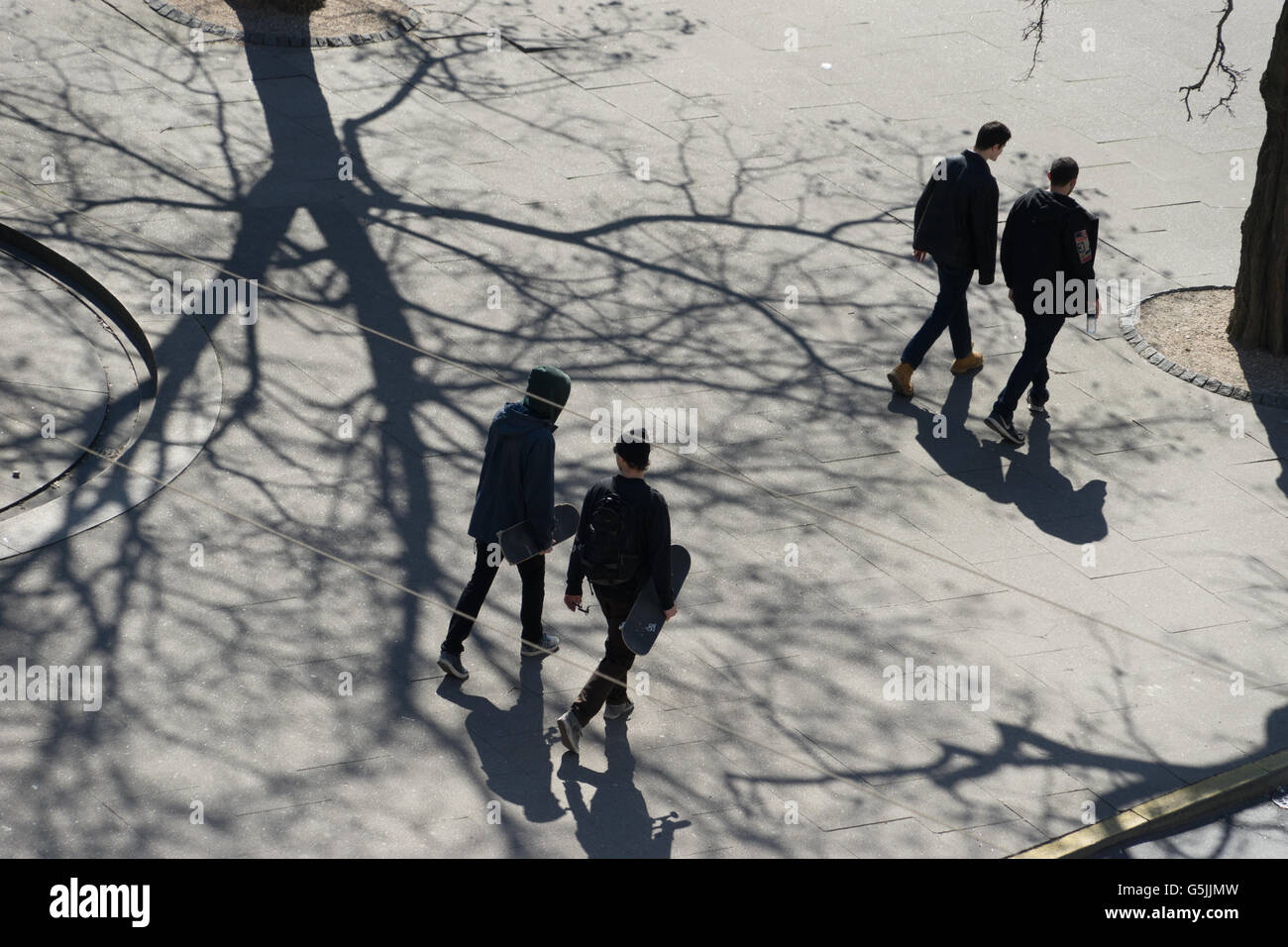Square with trees casting shadows, seen from above, four men walking ...