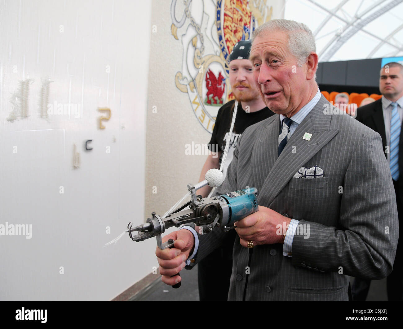The Prince of Wales uses a 'tufting gun' to work on a wool carpet ...
