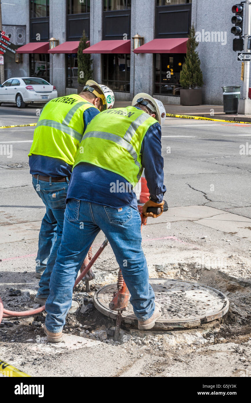Construction workers use jackhammer to expose manhole in street in ...