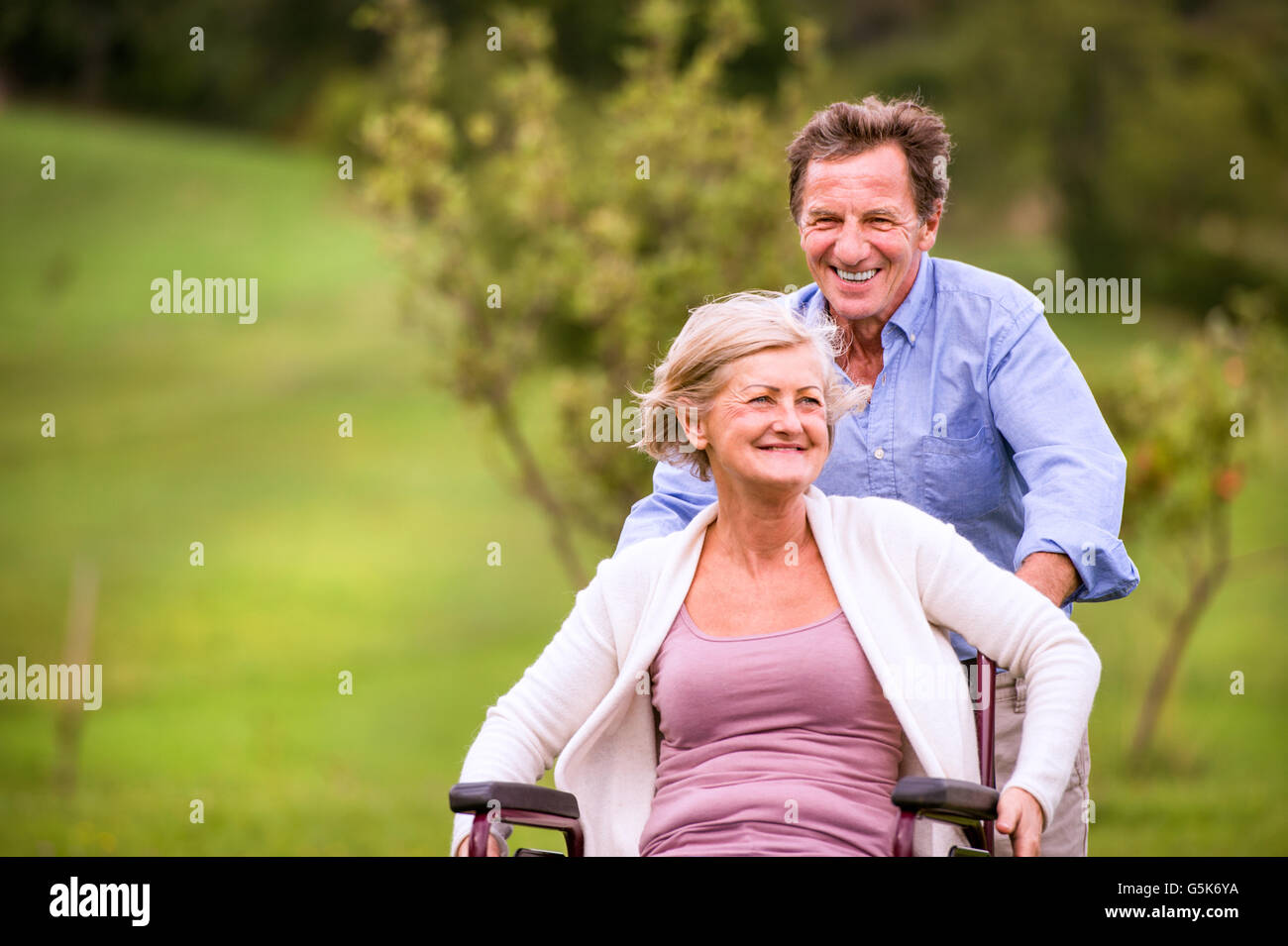 Senior man pushing woman in wheelchair, green autumn nature Stock Photo ...