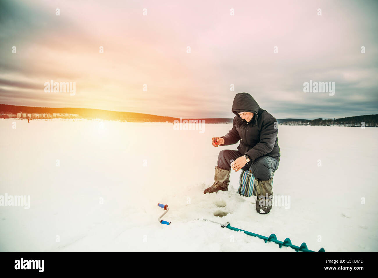Man ice fishing in frozen lake Stock Photo - Alamy