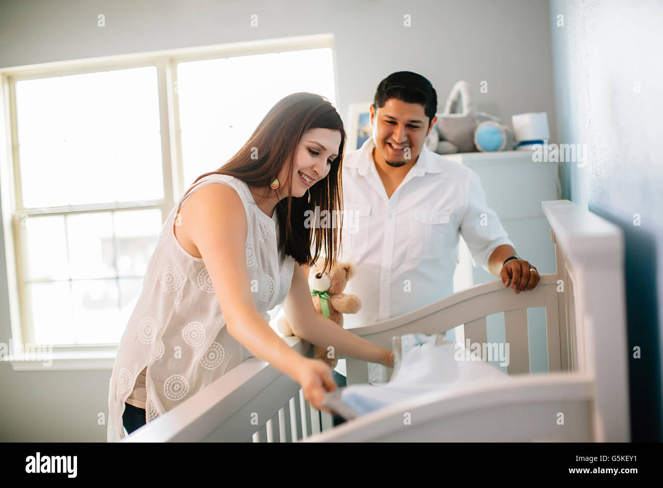 Hispanic couple preparing crib bed in nursery Stock Photo - Alamy