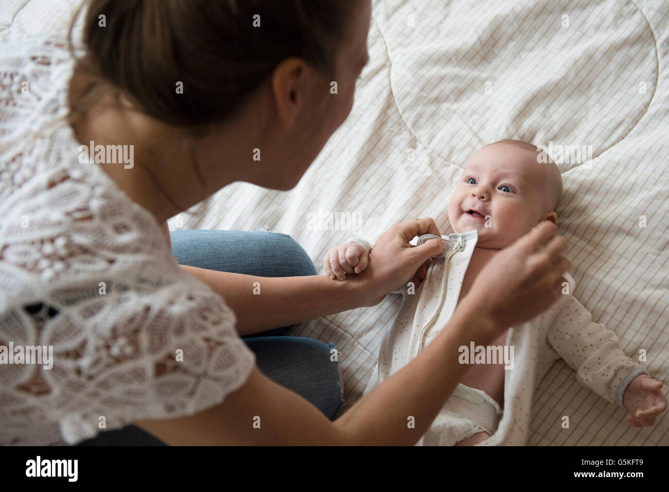 Caucasian mother dressing baby on bed Stock Photo - Alamy