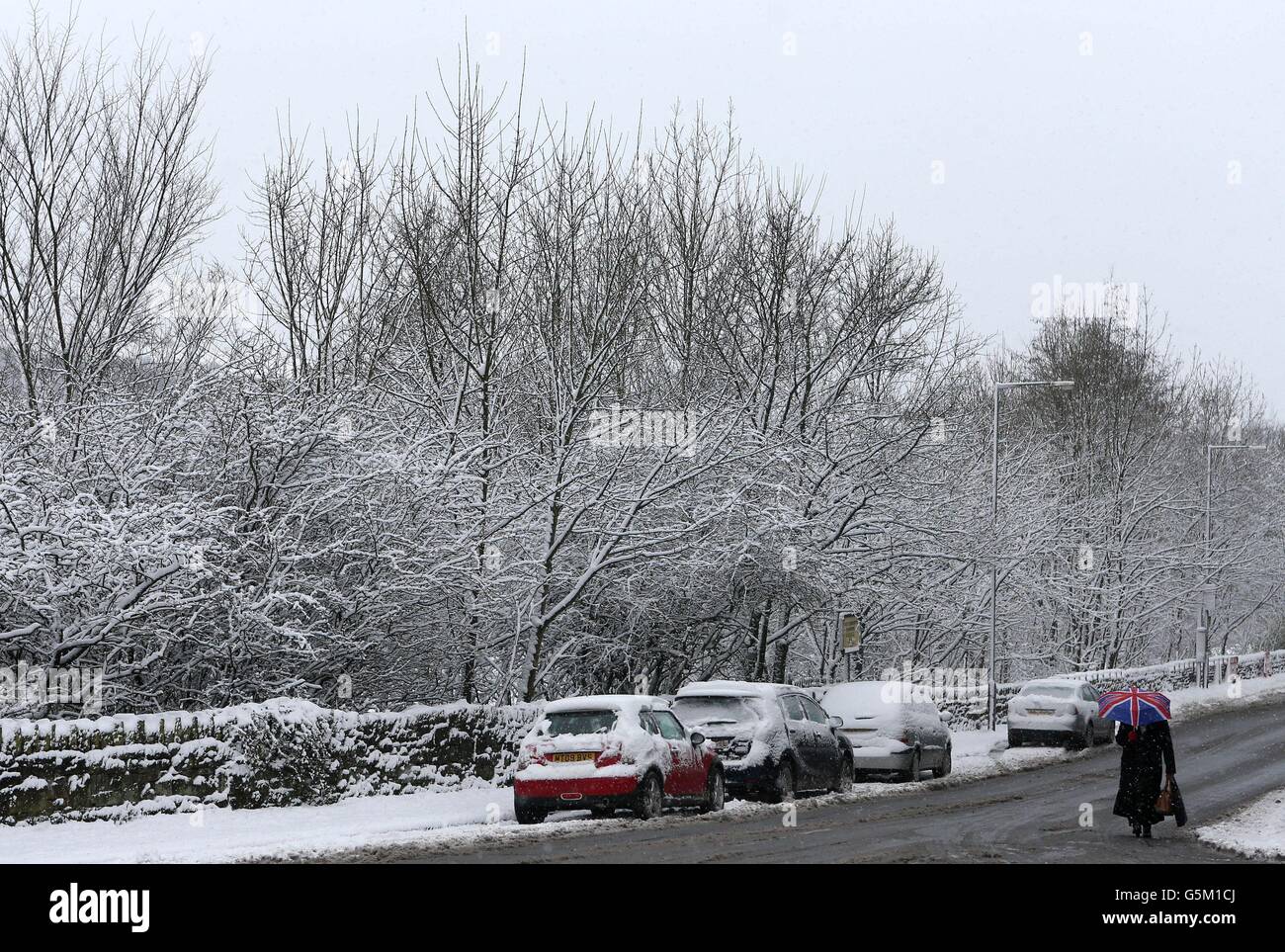 A woman walks in the road to avoid slipping on snow covered pavements ...