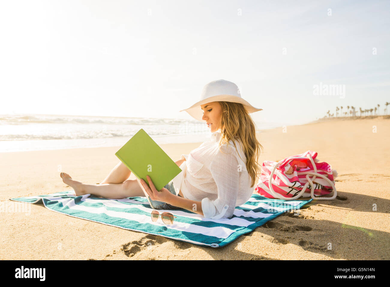 Caucasian woman reading book on beach Stock Photo - Alamy