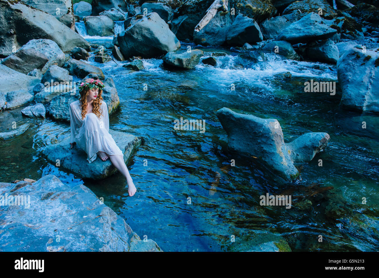 Caucasian woman wearing flower crown on rock at river Stock Photo - Alamy