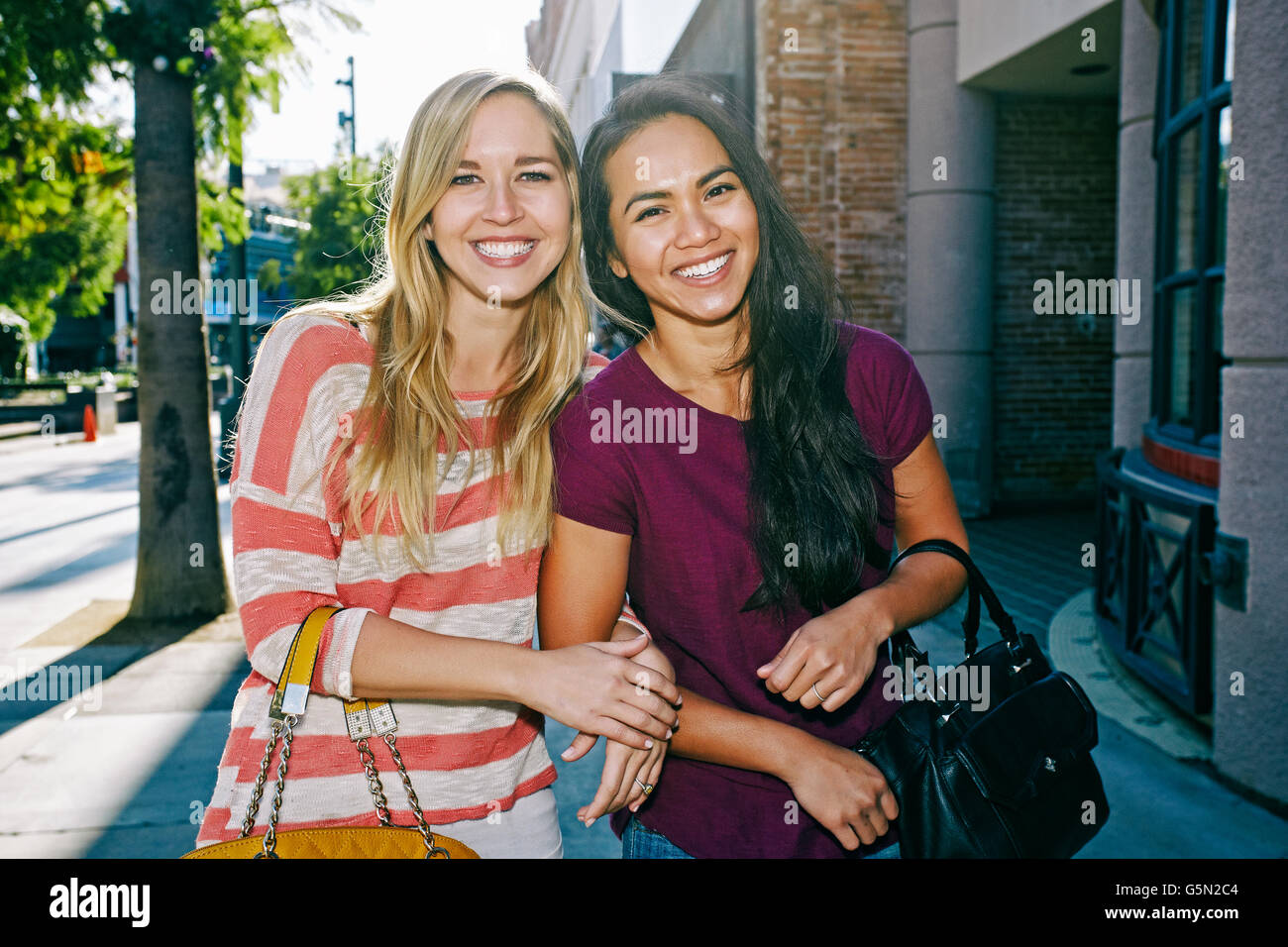 Women walking arm-in-arm on sidewalk Stock Photo - Alamy