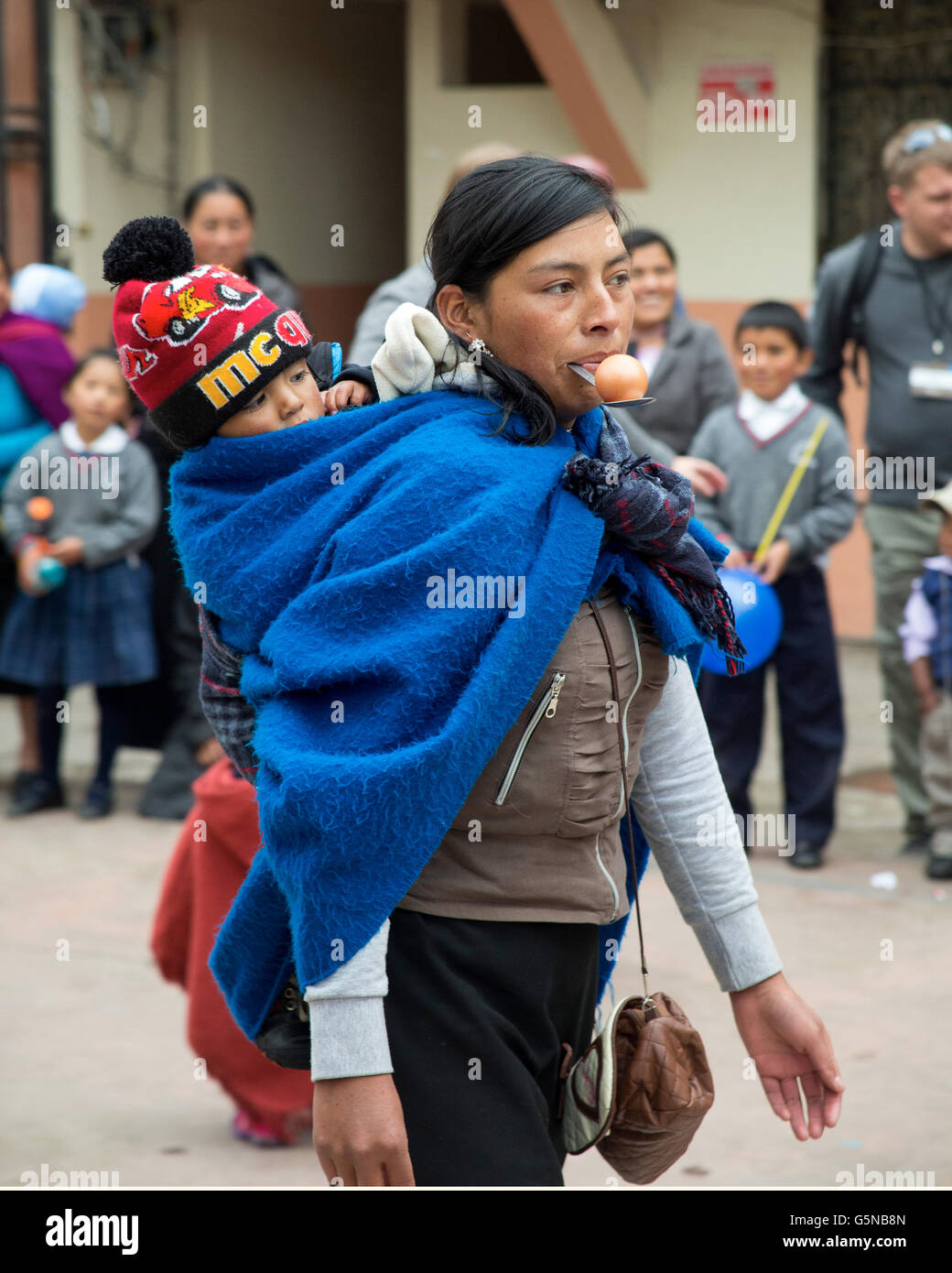 Ecuadorian woman carries her child on her back while balancing a spoon ...