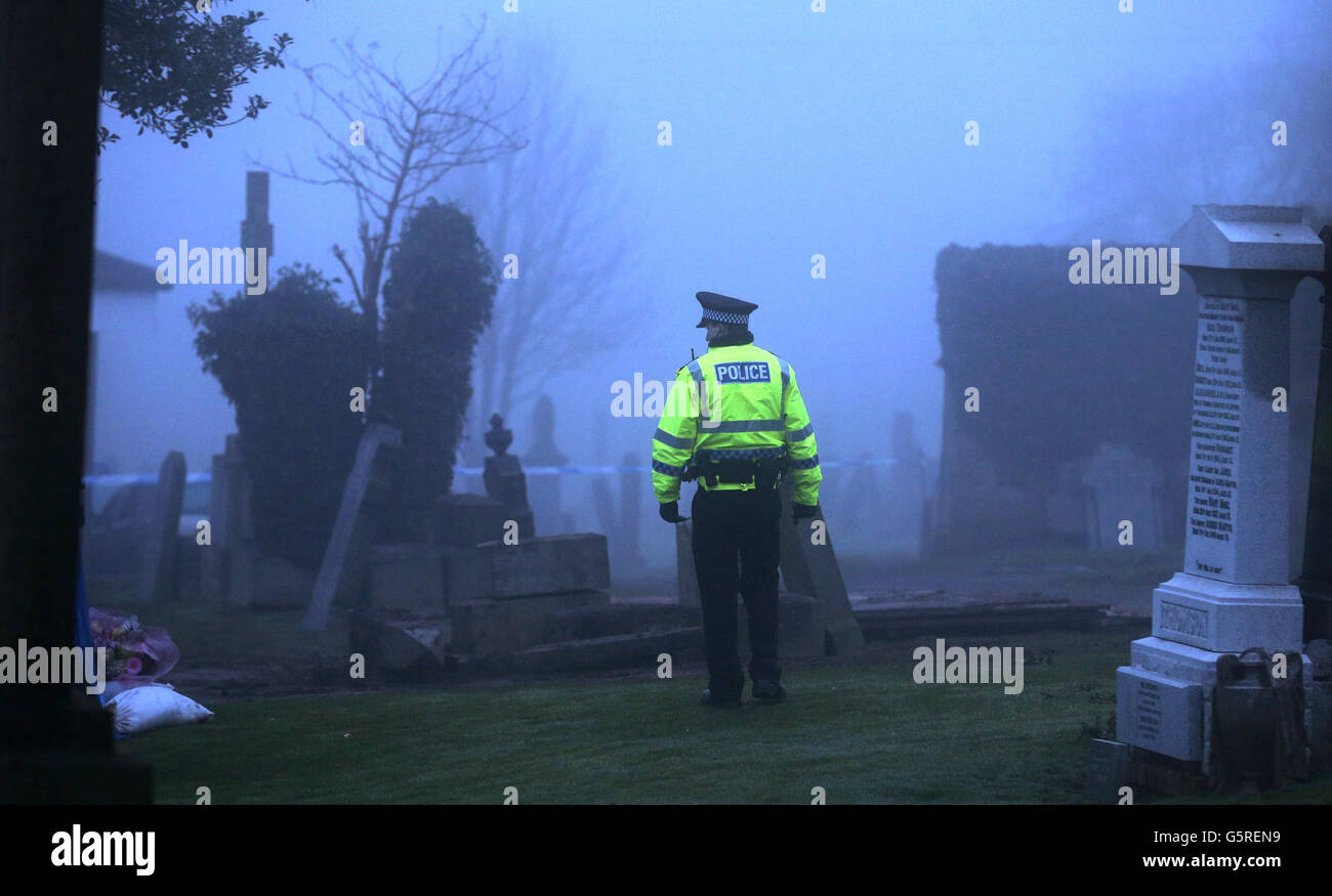 A police officer views flowers left at the scene at Old Monkland ...
