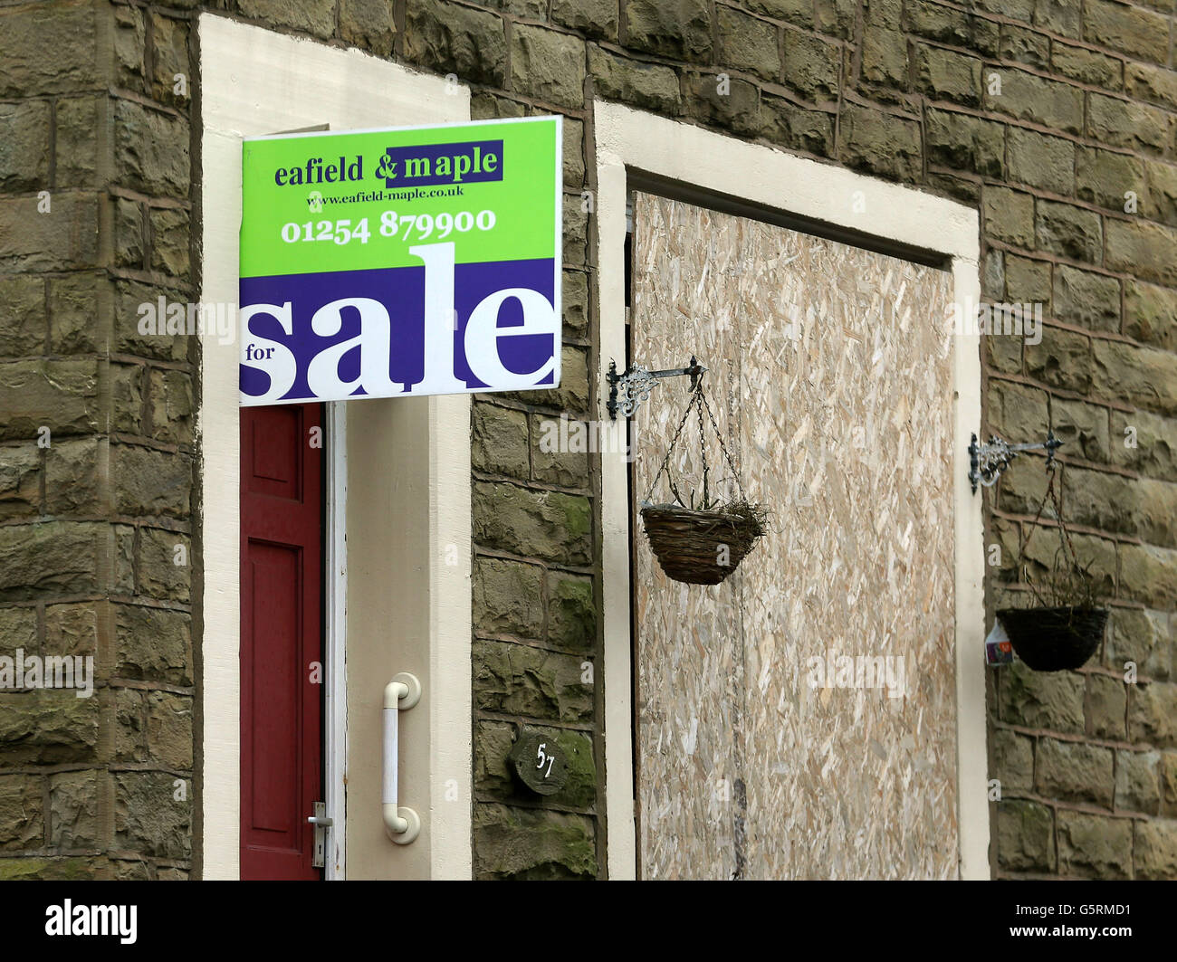Dead hanging baskets hang outside a boarded up house on a street in ...
