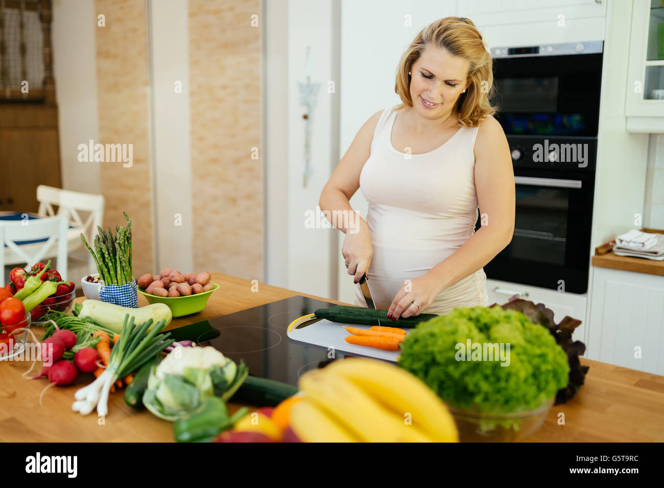 Beautiful pregnant woman preparing meal on kitchen island from fresh ...