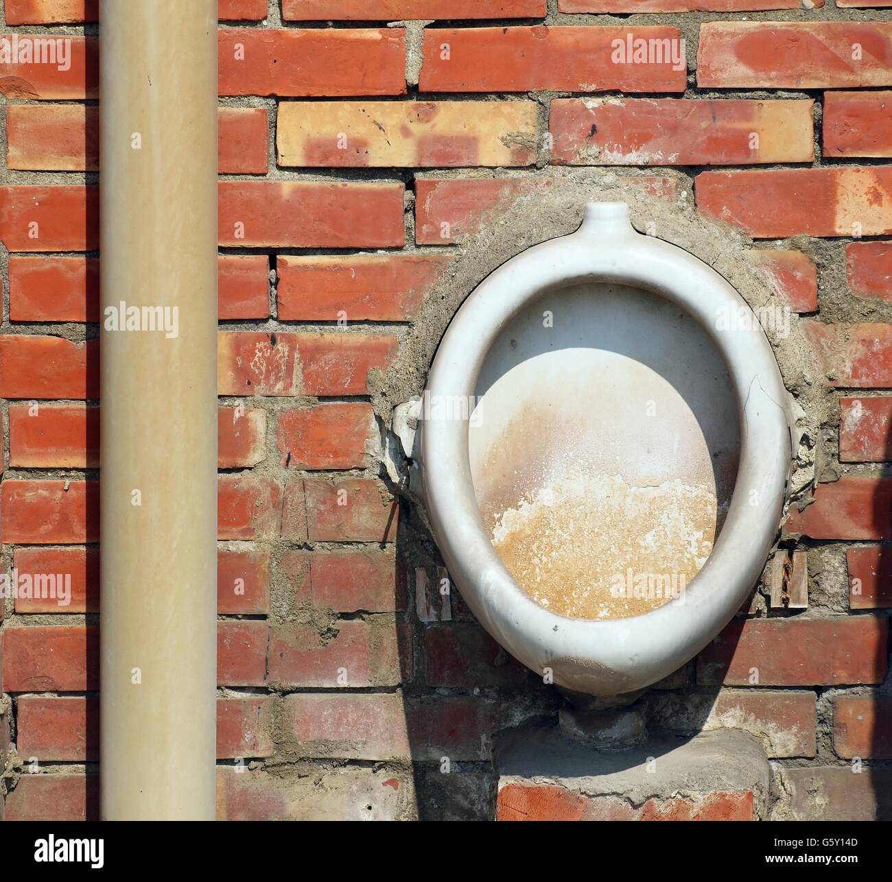 An old ceramic urinal bowl is mounted on a brick wall Stock Photo - Alamy