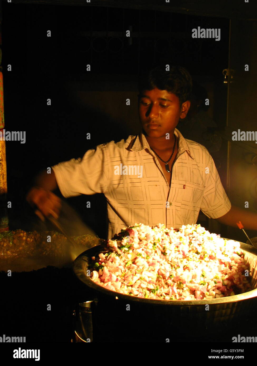 A poor young boy preparing food to sell on his roadside stall in India ...