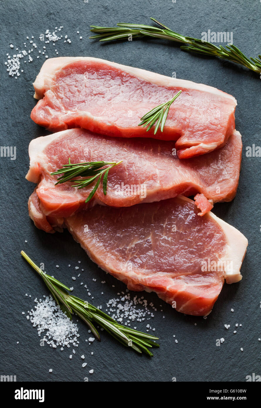 Raw pork steaks with rosemary on black stone background Stock Photo - Alamy