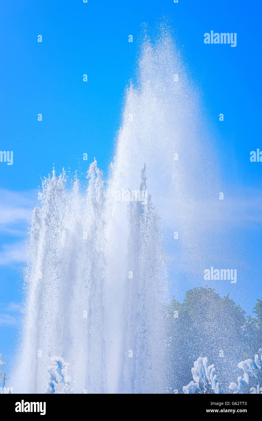 Fountain jet and water spray at sunny day against blue sky and distant ...