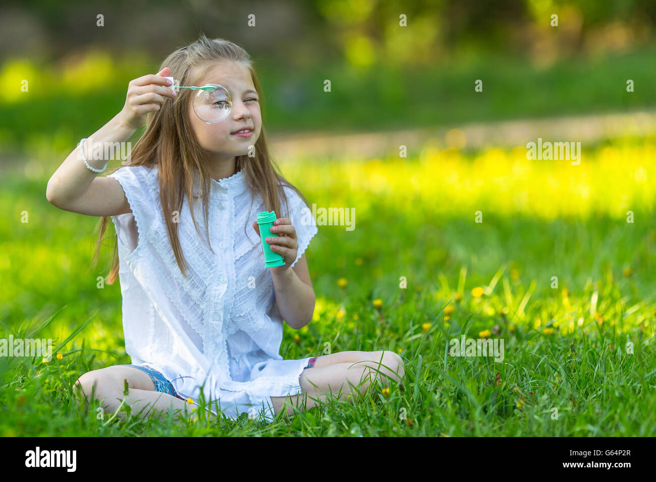 Little girl sitting in the grass and make blowing bubbles Stock Photo ...