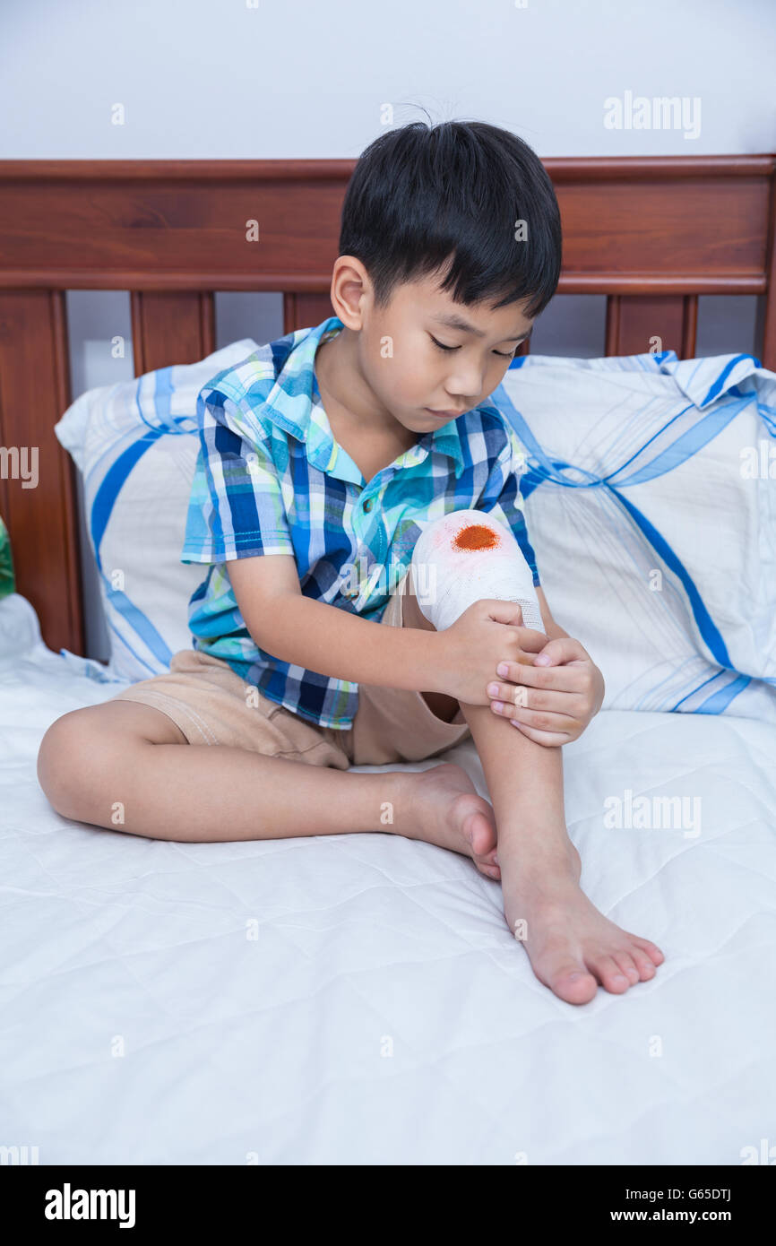 Child injured on bed in bedroom. Asian handsome boy looking at wound on ...