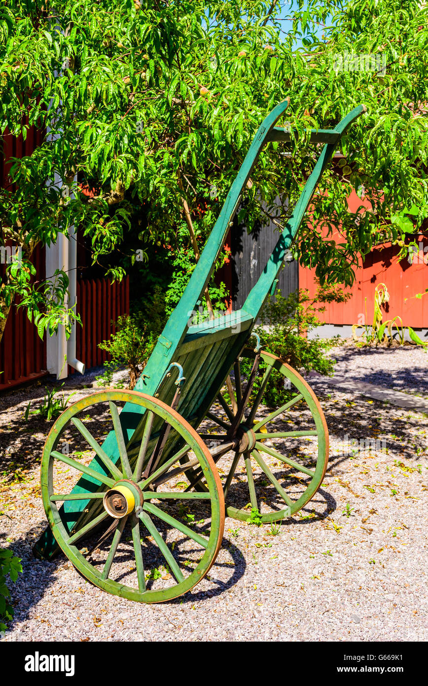 Green wooden handcart standing upright on gravel with a fruit tree in ...