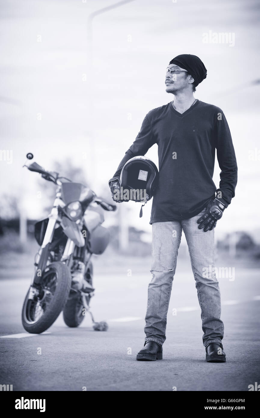 portrait of man biker standing on road with motorcycle in sunset ...