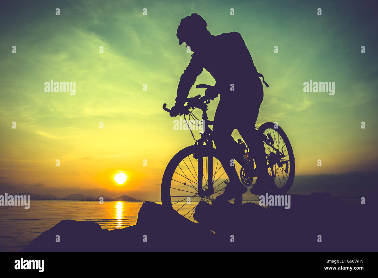 Silhouette of bicyclist riding the bike on a rocky trail at seaside, on ...