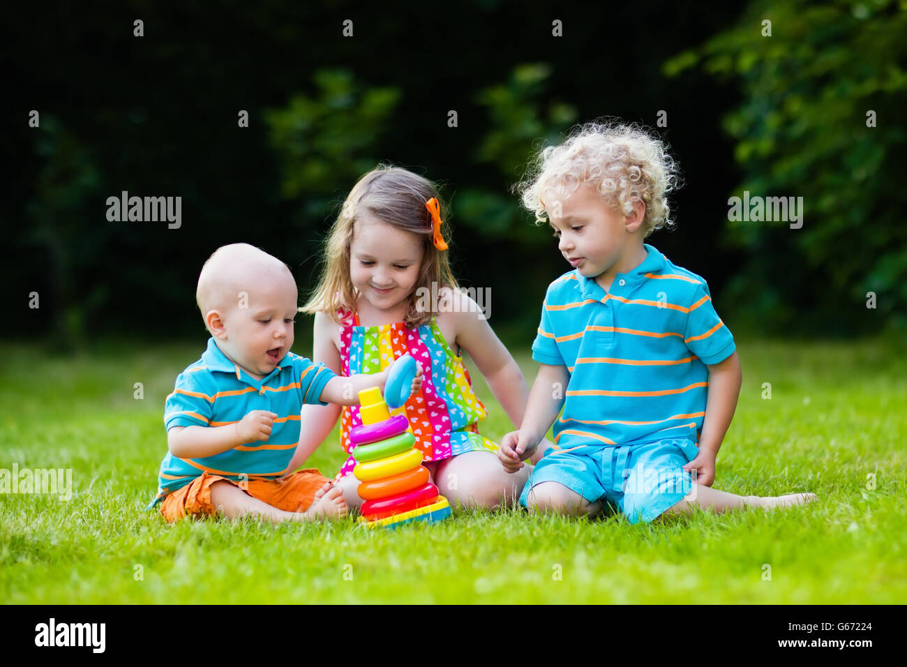 Three little children play with colorful rainbow pyramid toy ...