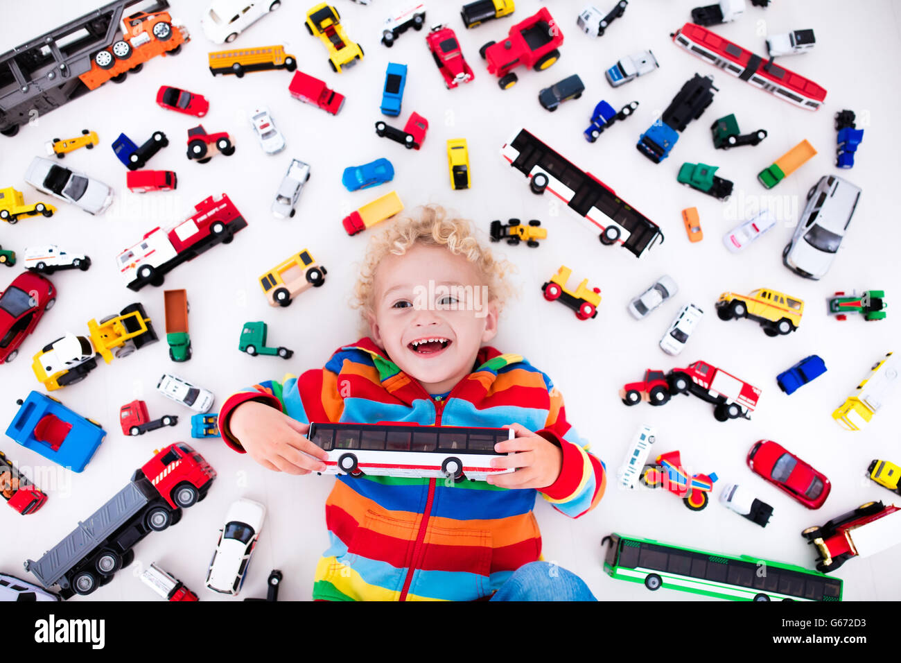 Funny curly toddler boy playing with his model car collection lying on ...