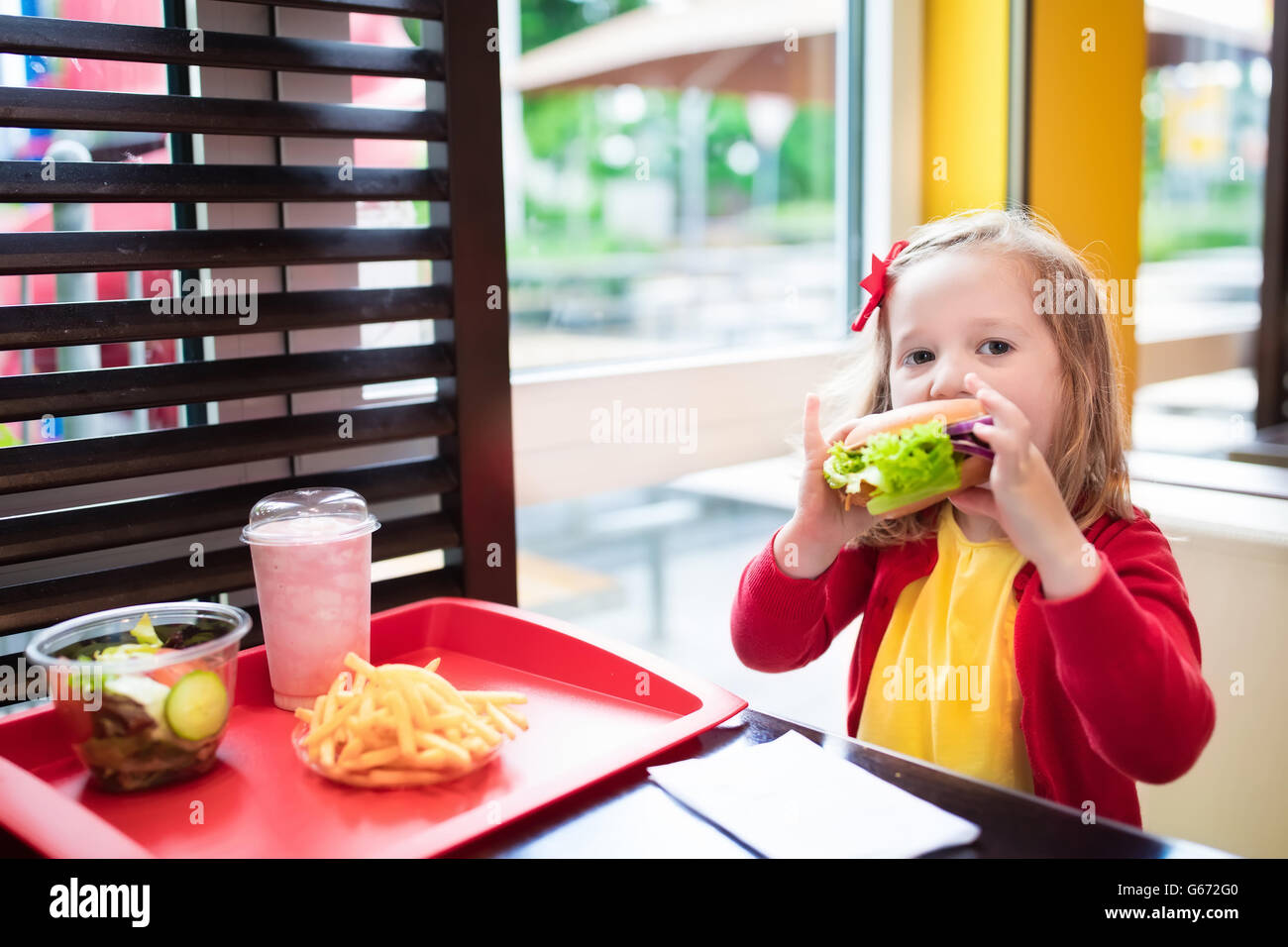 Little girl and boy eating chicken nuggets, hamburger and French fries ...