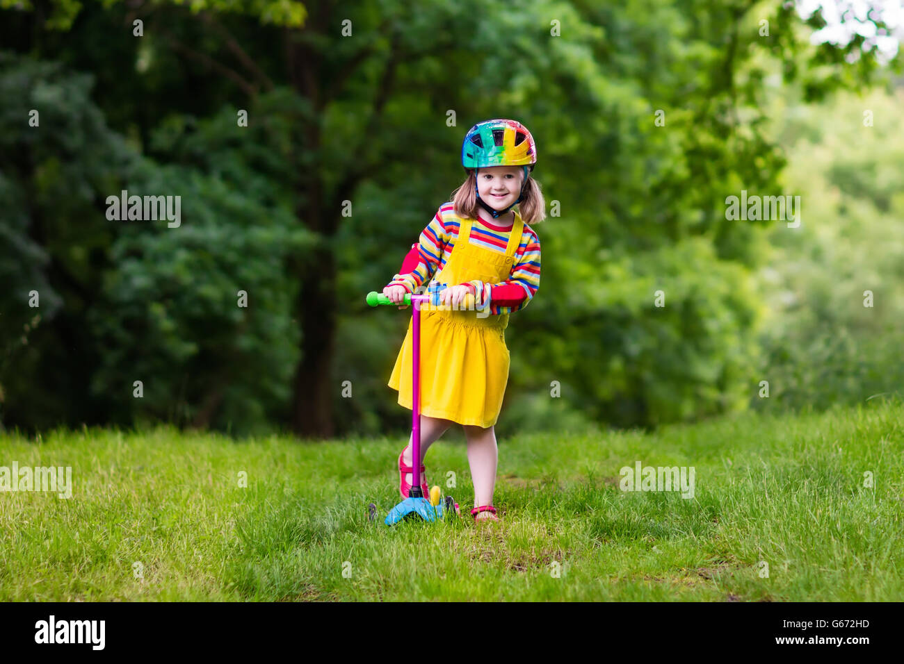 Little child learning to ride a scooter in a city park on sunny summer ...