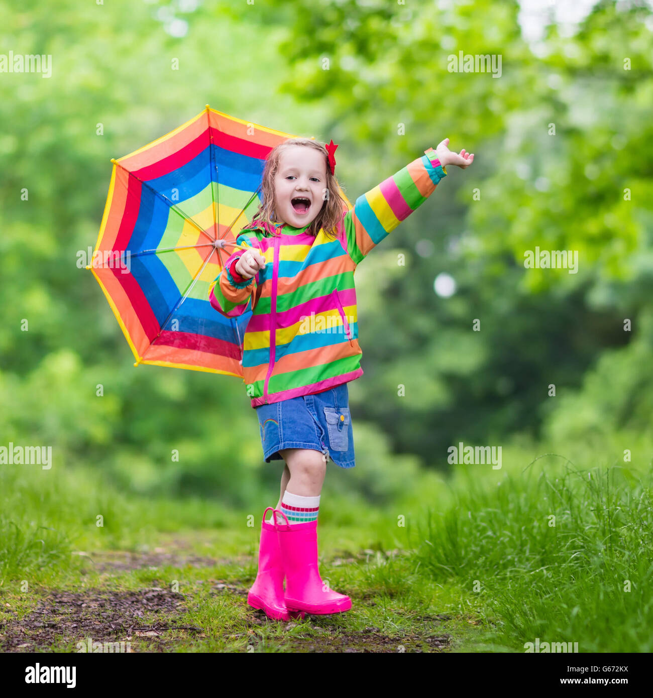 Little girl playing in rainy summer park. Child with colorful rainbow ...