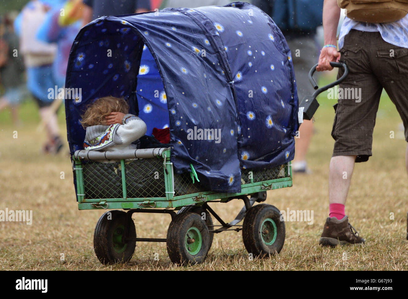 A young festival goer covers his ears from the loud music as rain falls ...