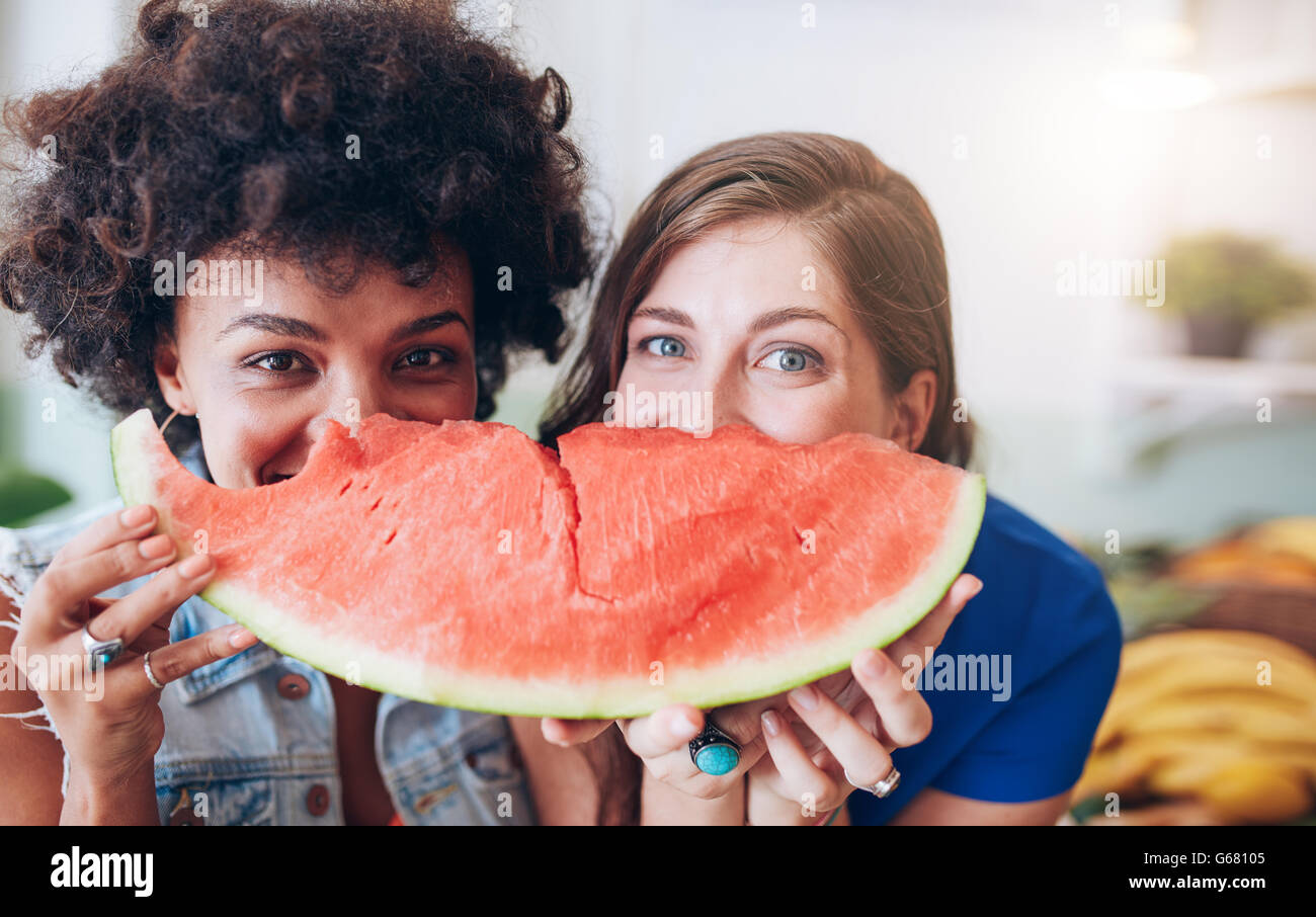 Two young women holding slice of watermelon and smiling while together ...