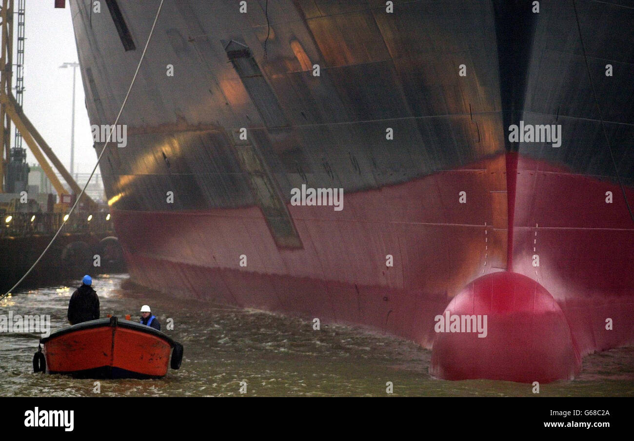 A tugboat alongside the Queen Mary 2 as she floats for the first time ...
