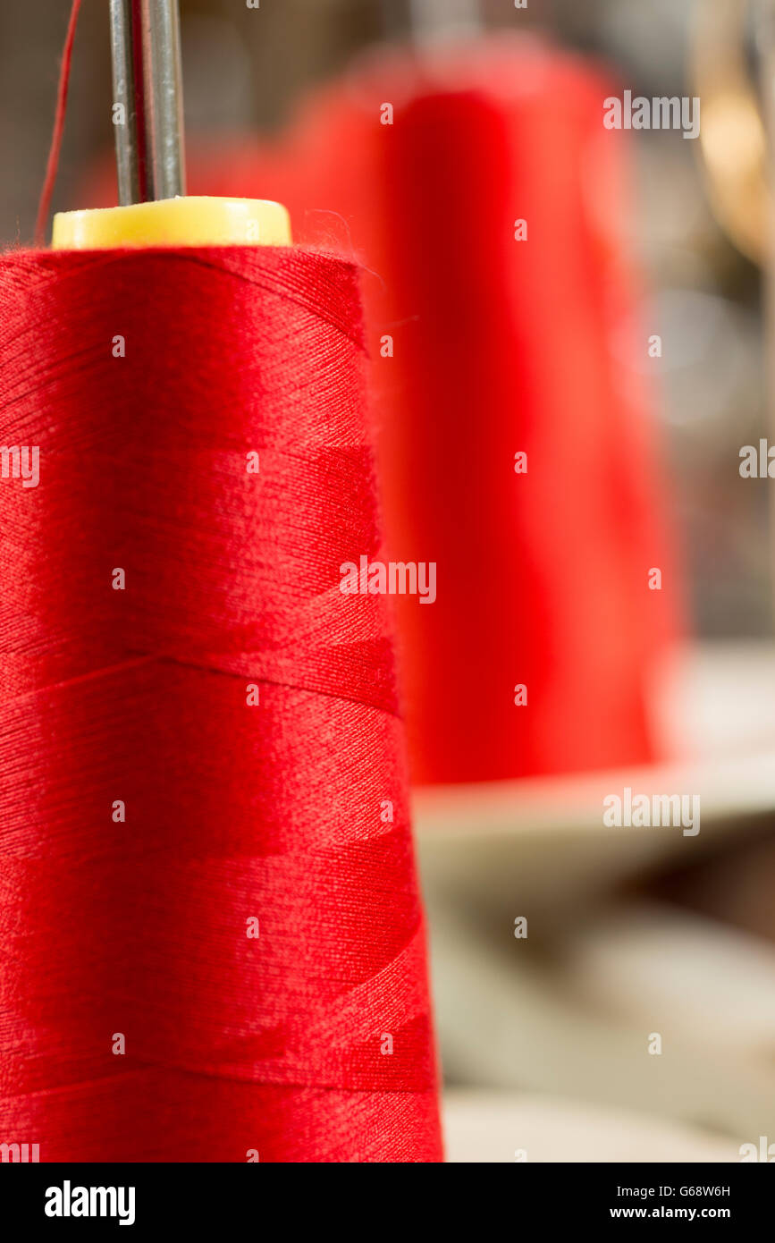 A spool of red thread on sweing machine pin with another spool of red ...