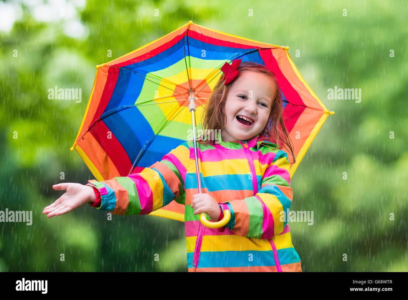 Little girl playing in rainy summer park. Child with colorful rainbow ...