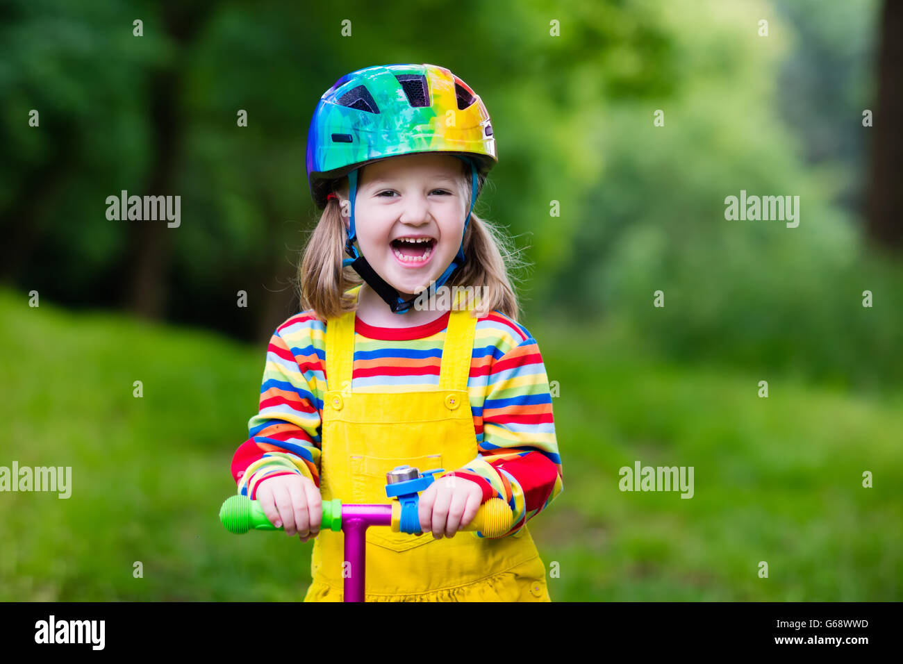 Little child learning to ride a scooter in a city park on sunny summer ...