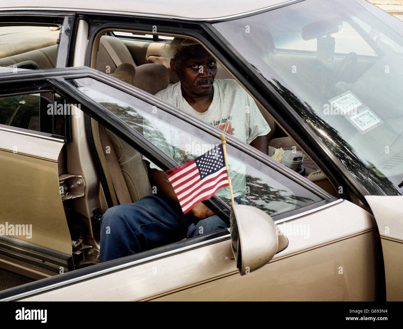man sitting in his car and a flag of United States on the mirror's car ...