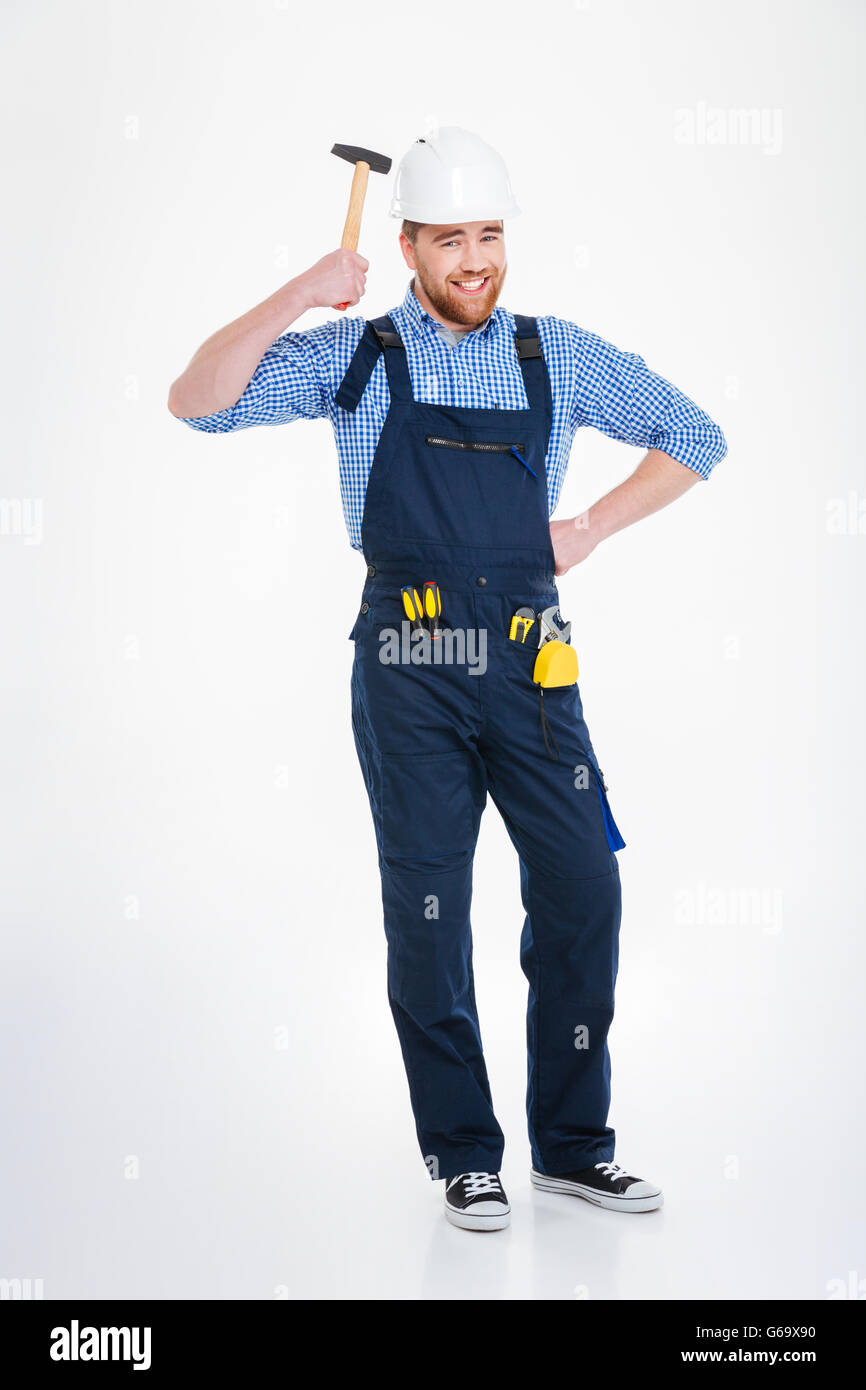 Smiling funny young builder applying hummer to his head in helmet and ...