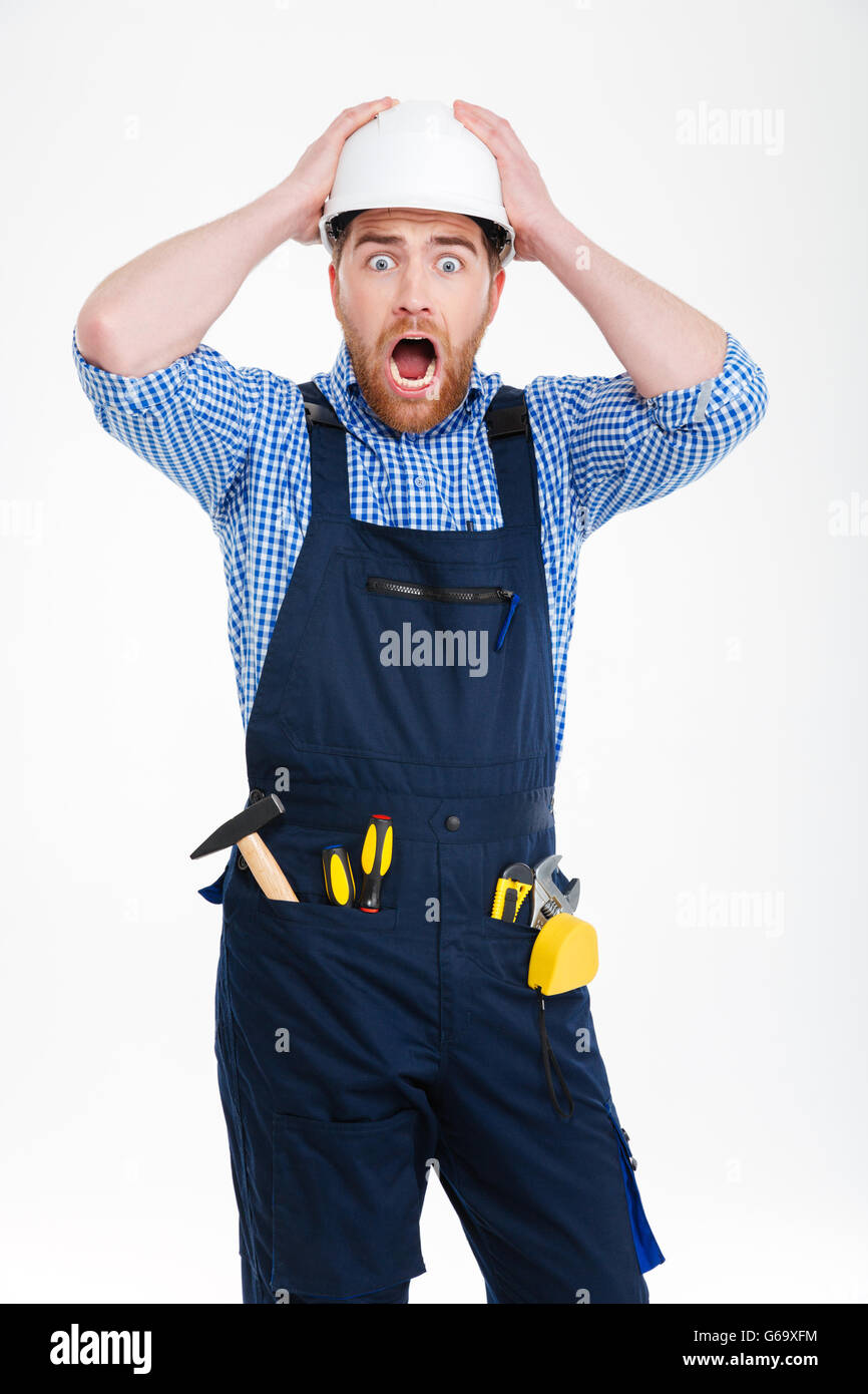 Astonished shocked young builder in helmet staning with mouth opened ...
