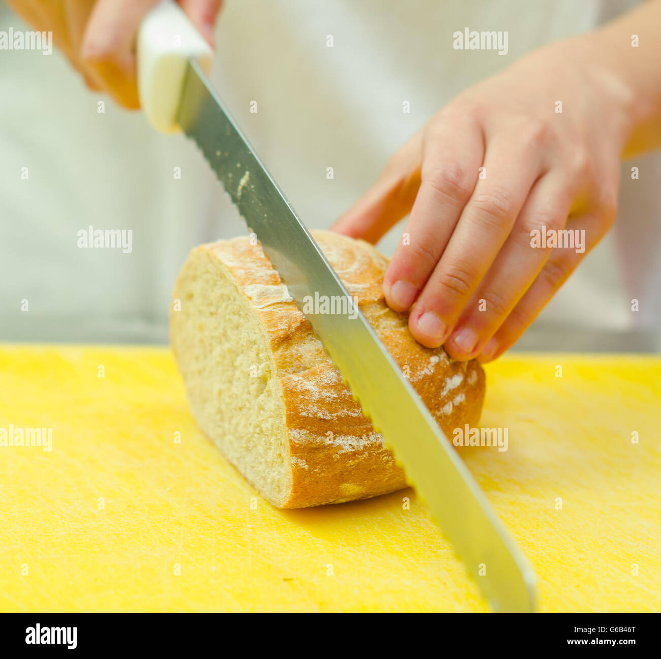 Cutting slices from loaf of bread sitting on yellow surface, hand ...